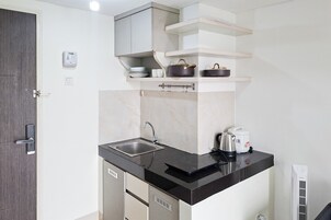Uma cozinha compacta com bancada preta, pia embutida, cafeteira e micro-ondas.