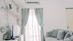 Quarto com cama, escrivaninha com computador, ar condicionado e janela com cortinas.