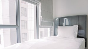 Quarto de hotel com cama, janela com persianas e vista para edifícios.