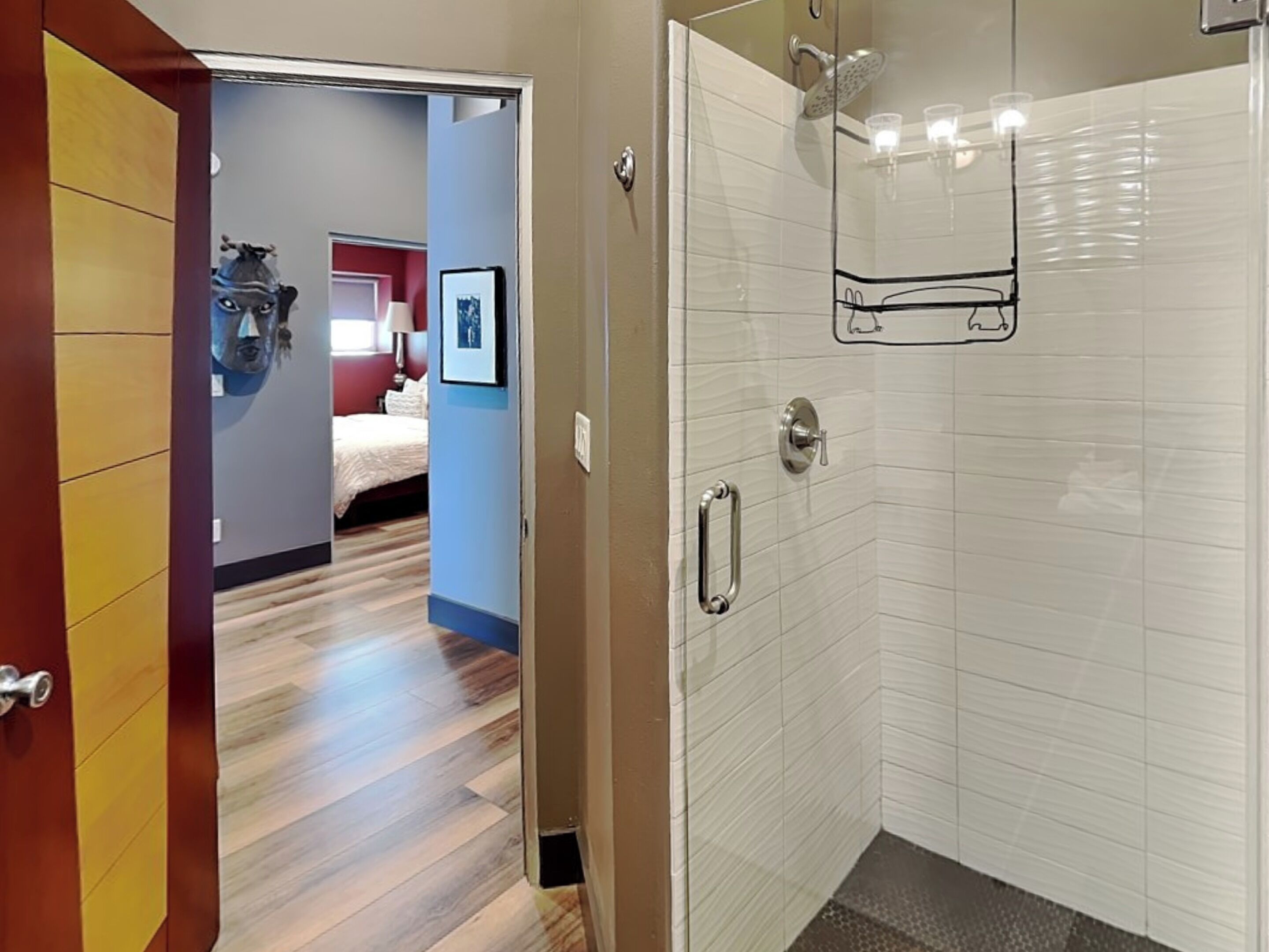 Quarto de hotel com chuveiro, uma cama e um corredor que dá para outro quarto.