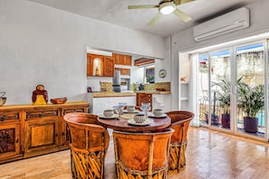 Uma sala de jantar com uma mesa redonda, cadeiras de madeira e uma cozinha ao fundo.