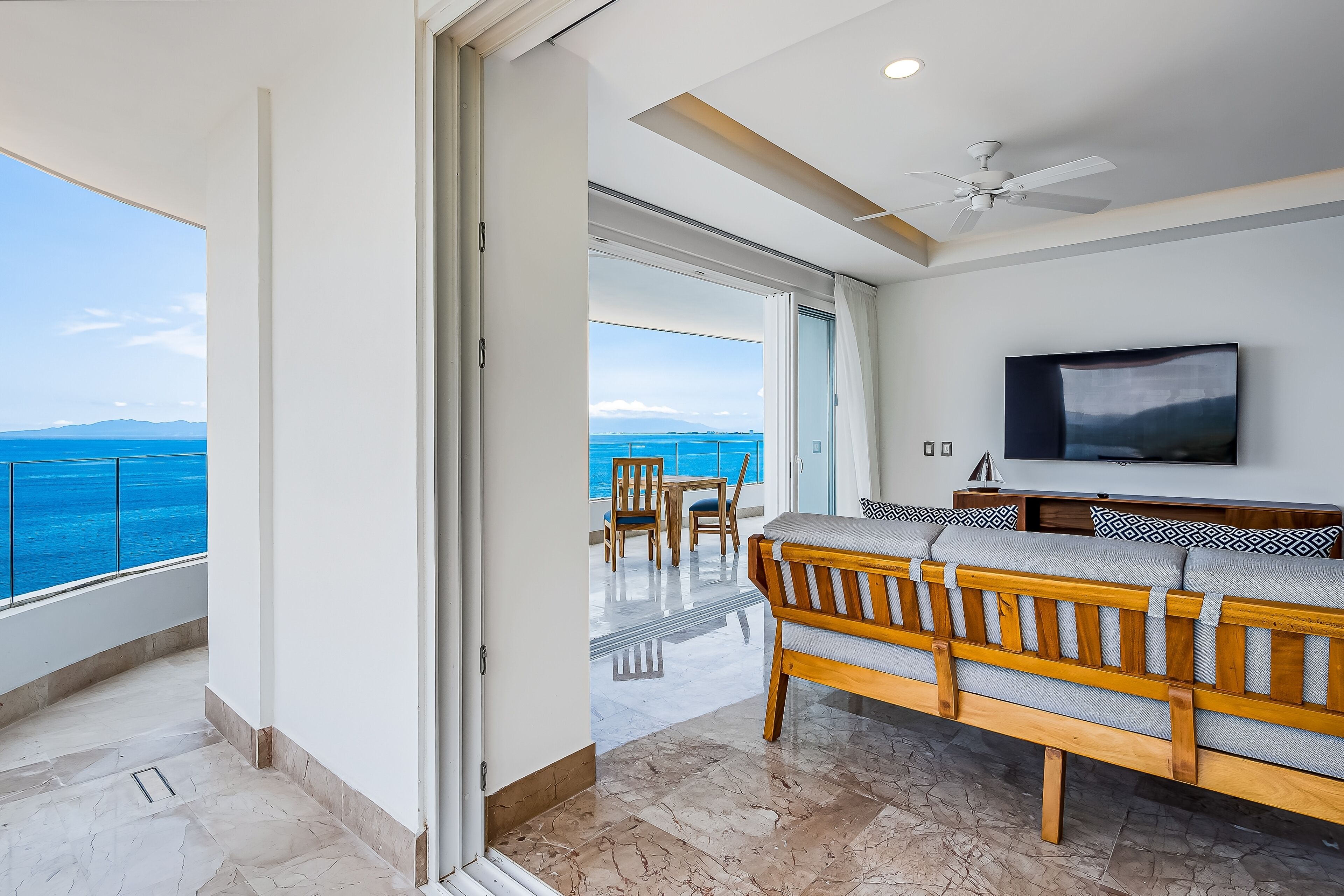 Uma sala de estar moderna com sofá, TV e varanda com vista para o mar.