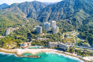 Um resort à beira-mar com villas na praia, um hotel central e montanhas ao fundo.