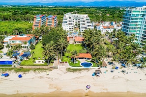 Um resort com vários edifícios, praia, palmeiras e piscina.