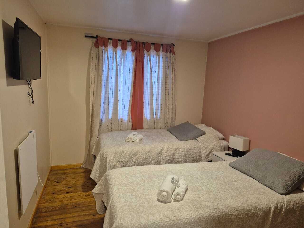 Quarto com duas camas, televisão, radiador e janela com cortinas.