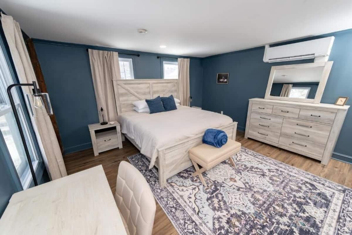 Quarto com cama, mesa de cabeceira, banco, cômoda e ar condicionado.