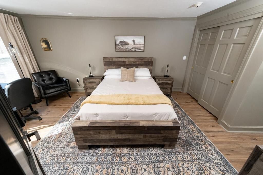 Quarto com cama de madeira, uma escrivaninha, uma cadeira e um guarda-roupa.