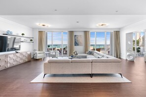 Uma sala de estar moderna com um amplo sofá modular, uma TV de tela plana e vista para o oceano.