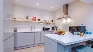 Uma cozinha moderna com ilha central, eletrodomésticos embutidos e um suporte para panelas suspenso.