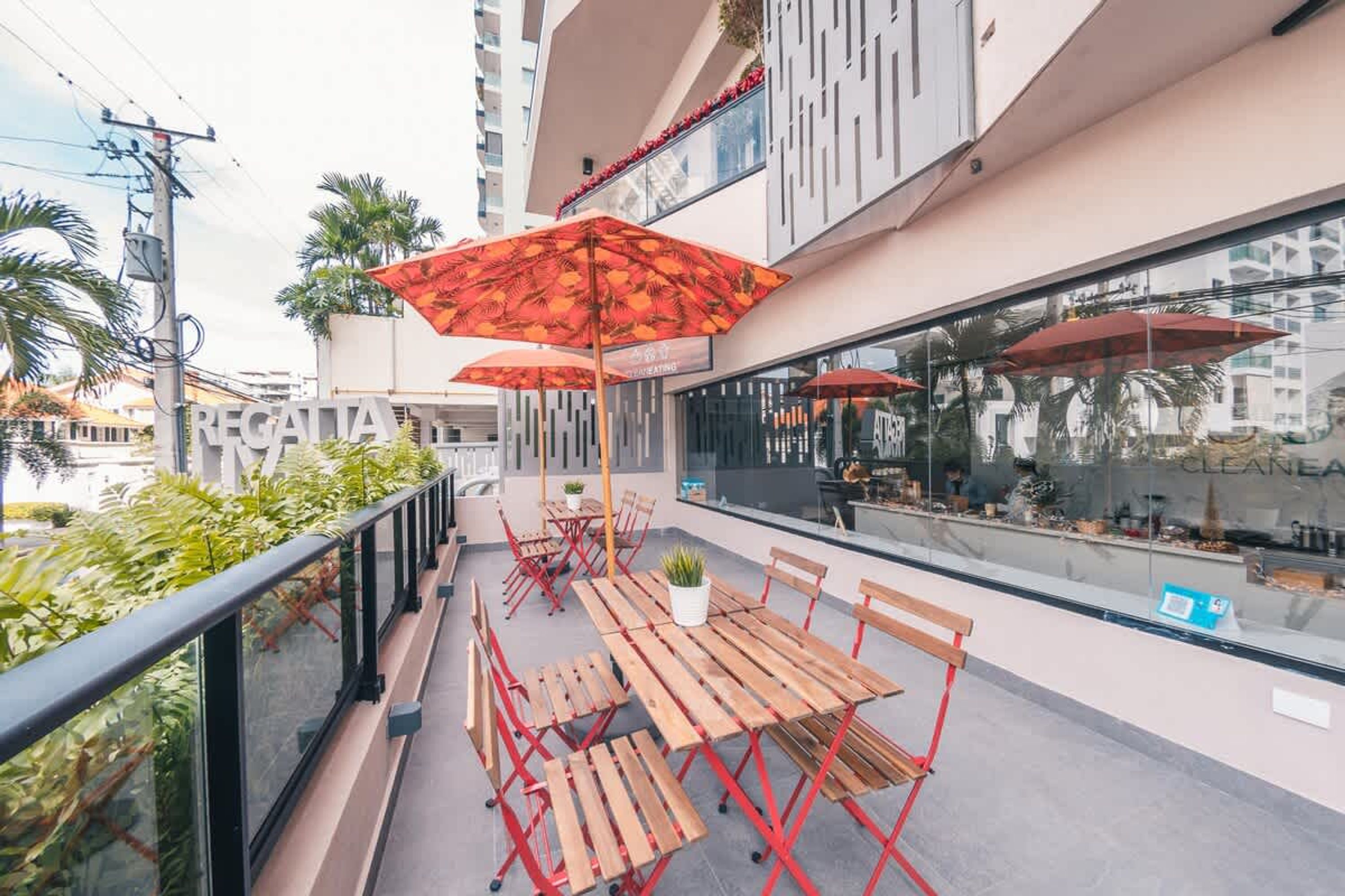 Terraço no telhado com mesas de madeira e guarda-sóis vermelhos, com vista para a paisagem urbana.