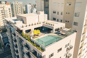 Um edifício moderno com piscina no terraço, varandas e área de lounge envidraçada.