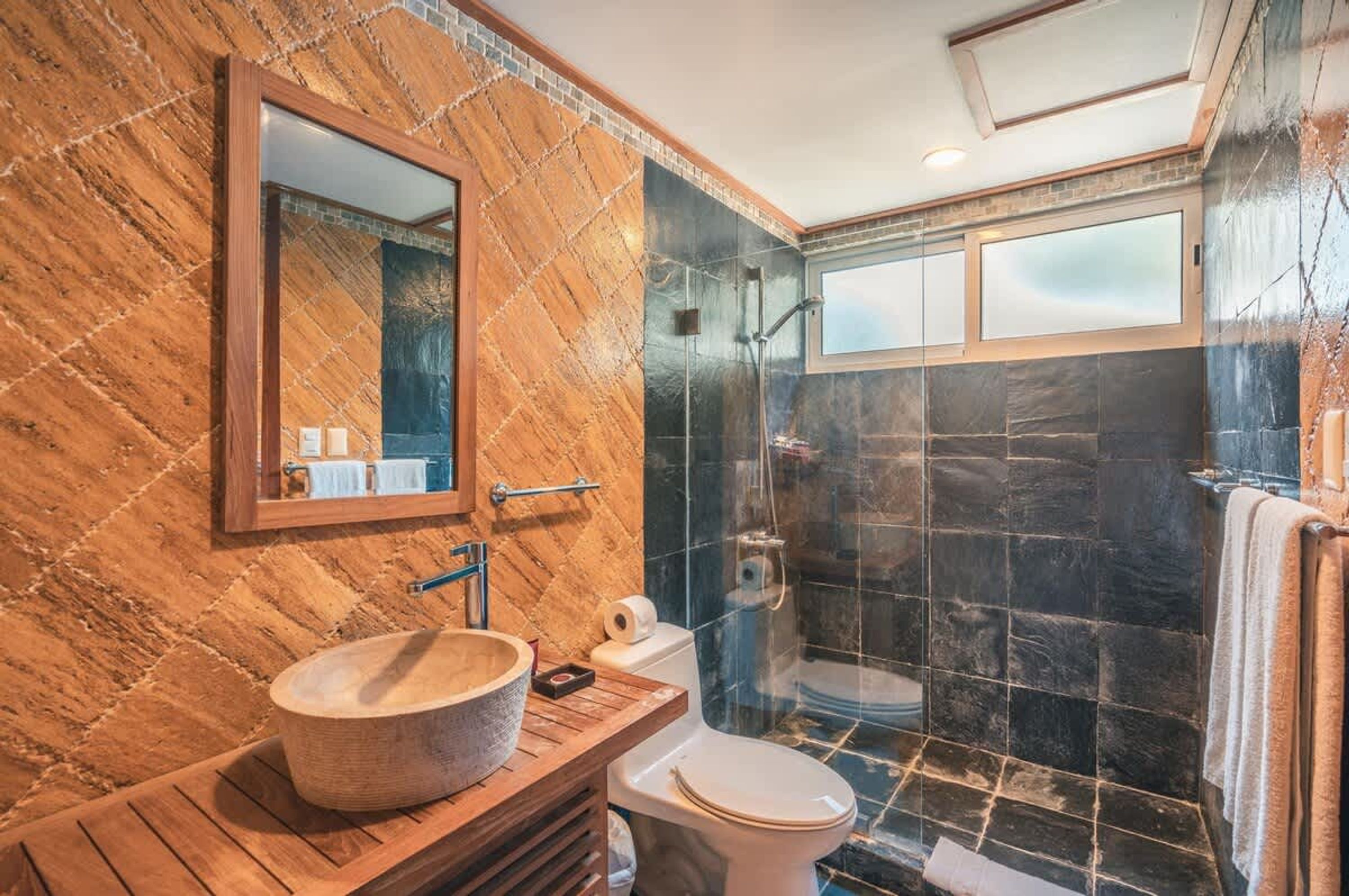 Uma casa de banho com toucador de madeira, um espelho grande, sanita e zona de duche.