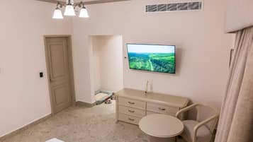 Um quarto com televisão na parede, uma mesinha redonda, um sofá, um armário e uma porta.