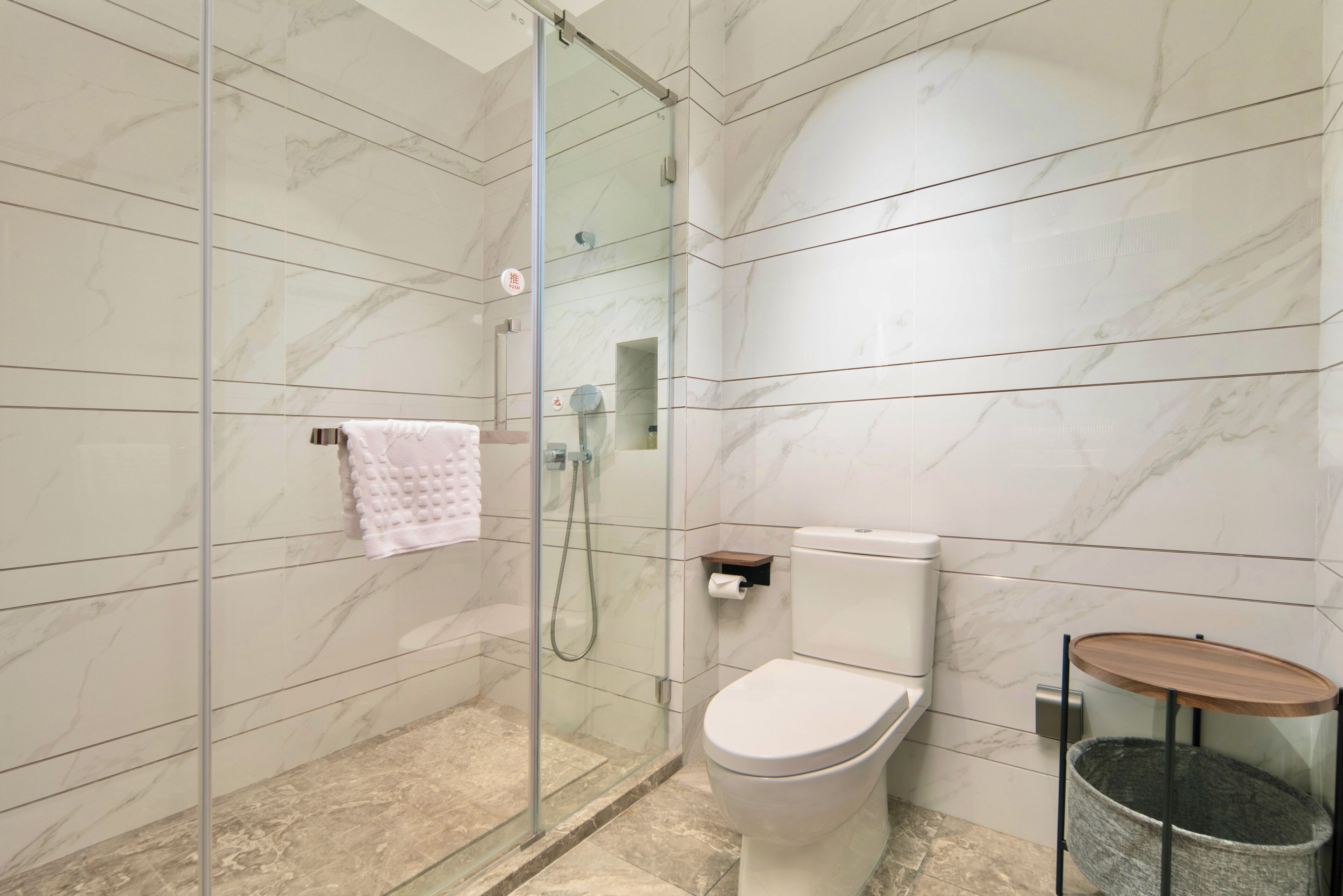 Um banheiro moderno com chuveiro em gabinete de vidro, vaso sanitário e pequena mesa de madeira.