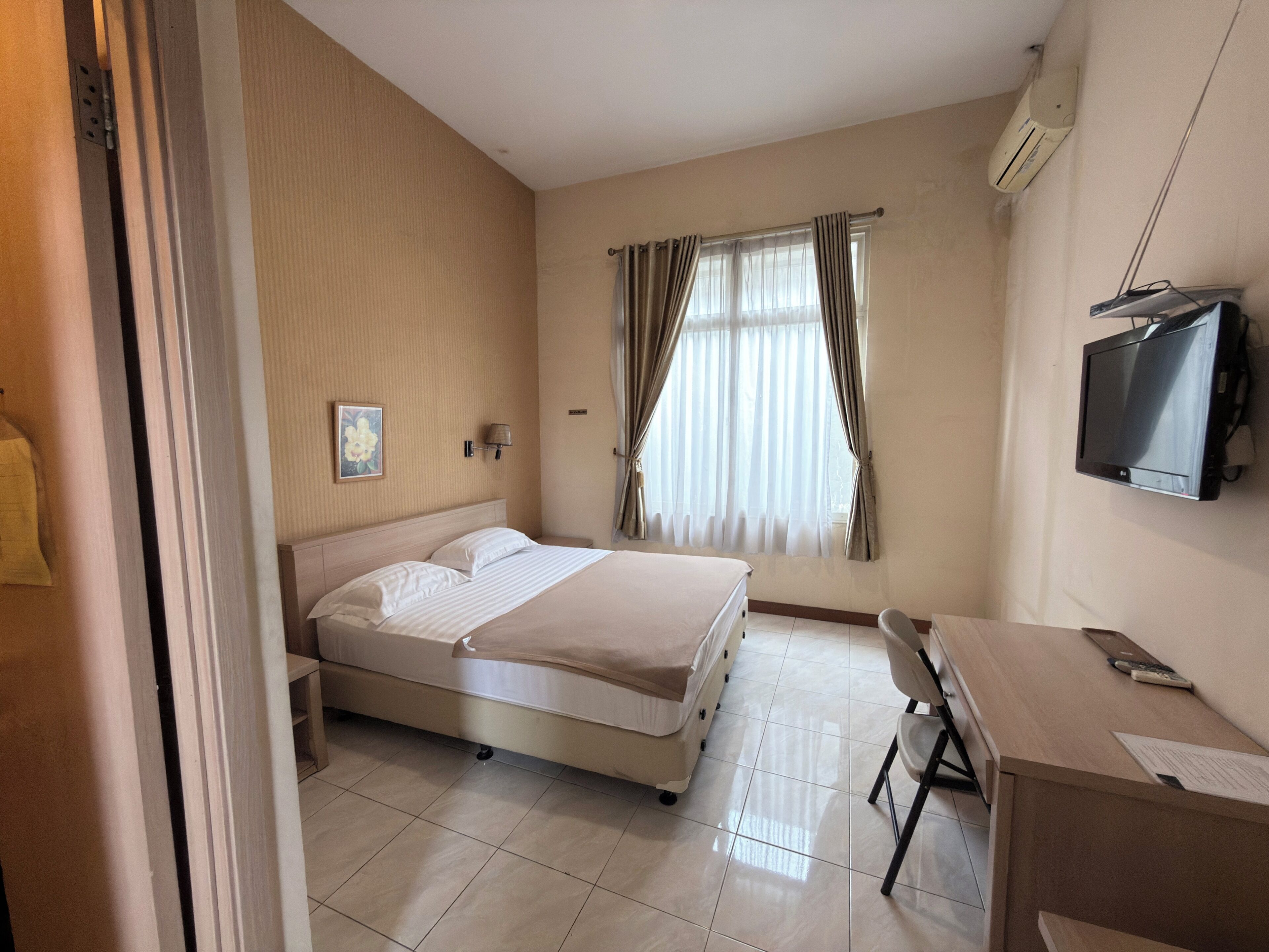 Quarto de hotel com cama, escrivaninha, televisão e janela com cortinas.