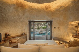 Quarto com cama, um banco de madeira, televisão e vista para a área da piscina.