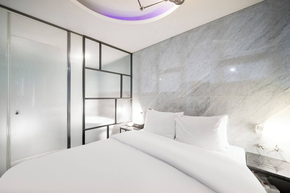 Quarto moderno com uma cama grande, uma divisória de vidro e cabeceira de mármore.