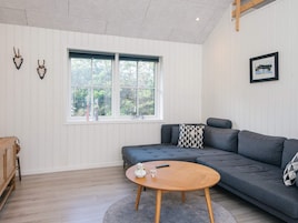 Sala de estar com sofá cinza, mesa de centro redonda de madeira e janela com vista para árvores.