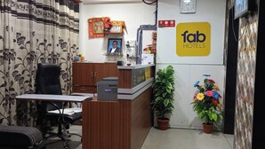 Área de recepção de hotel com balcão, cadeiras, relógio, planta e placa da Fab Hotels.