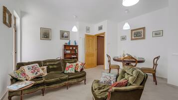 Uma sala de estar com um sofá verde, uma mesa de apoio de madeira e um espaço de jantar com uma mesa e cadeiras de madeira.