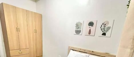 Um quarto com uma cama, um guarda-roupa de madeira e três obras de arte penduradas na parede.