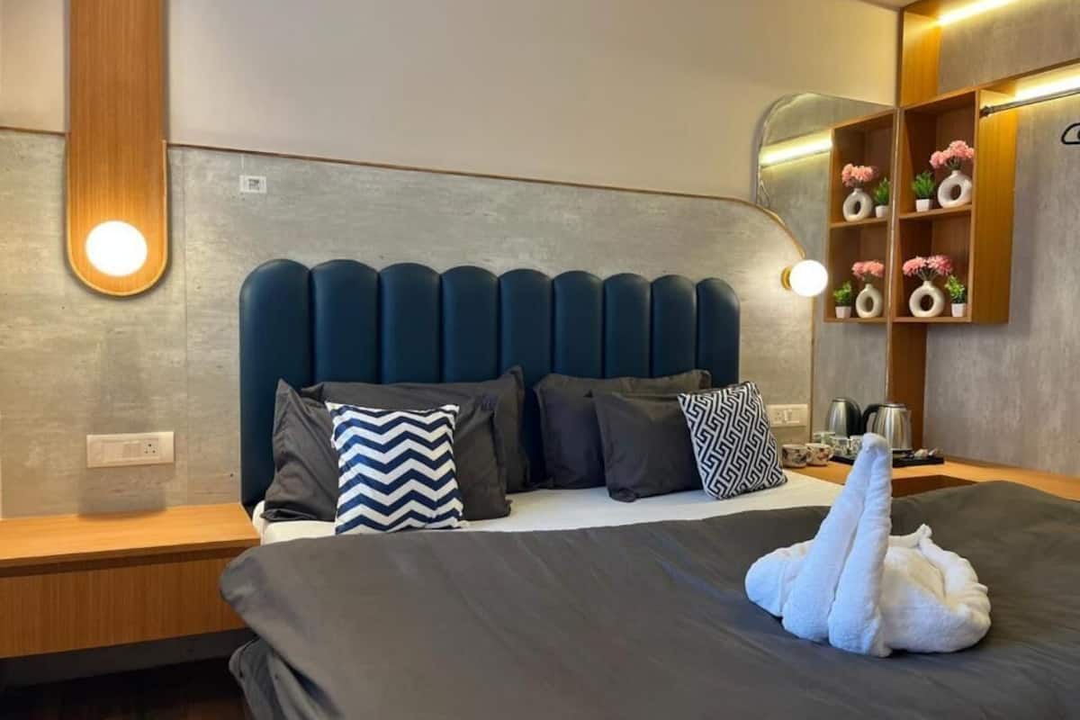 Quarto de hotel moderno com uma cama grande, mesa de cabeceira de madeira, prateleira na parede com objetos decorativos e cabeceira embutida.