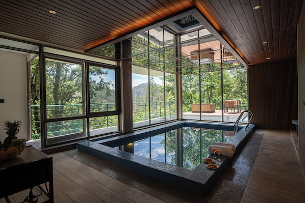 Piscina interior moderna com amplas janelas, teto de madeira e vista para o verde lá fora.