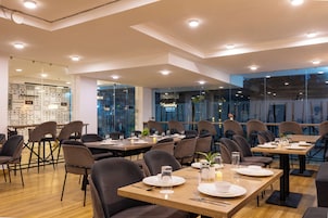 Um restaurante moderno com mesas preparadas para refeições, janelas amplas e vista para a paisagem urbana.