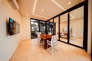 Uma sala de reunião moderna com uma mesa de madeira, cadeiras brancas, paredes de vidro e um aparelho de ar condicionado.