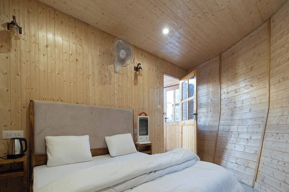 Quarto com painéis de madeira, uma cama, mesa de cabeceira, um ventilador e uma janela.