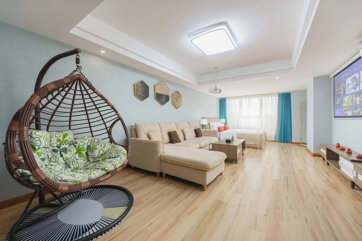 Uma sala de estar com uma cadeira suspensa, um conjunto de sofás, uma mesa de centro e uma tela de televisão.