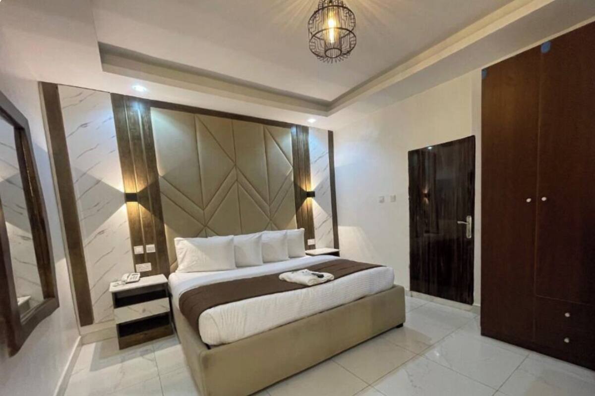 Quarto moderno com uma cama grande, mesas de cabeceira, guarda-roupa e um painel decorativo na parede.
