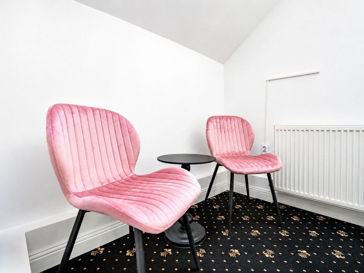 Um quarto com duas cadeiras estofadas rosa, uma mesa redonda pequena e um radiador na parede.