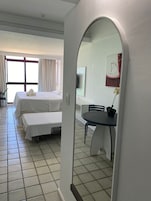 Quarto de hotel com duas camas, uma mesa de jantar e uma janela grande.