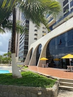 Um edifício moderno com grandes janelas, piscina e área de estar externa com guarda-sóis.