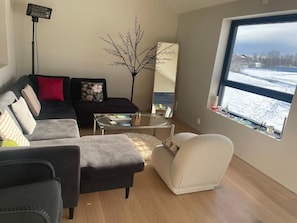 Uma sala de estar com sofá, poltrona, mesa de centro e uma janela grande com vista para uma paisagem nevada.