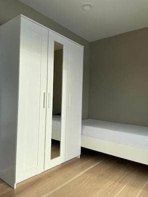Um quarto com um guarda-roupa branco, um banco e soalho de madeira.