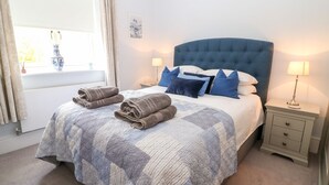 Quarto com uma cama grande, duas mesas de cabeceira, uma janela com cortinas e uma obra de arte na parede.