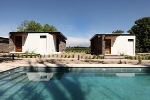 Uma área moderna à beira da piscina com duas cabanas pequenas, piscina cristalina e montanhas ao fundo.