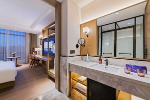 Quarto de hotel com cama, escrivaninha, cadeira e um espelho grande.