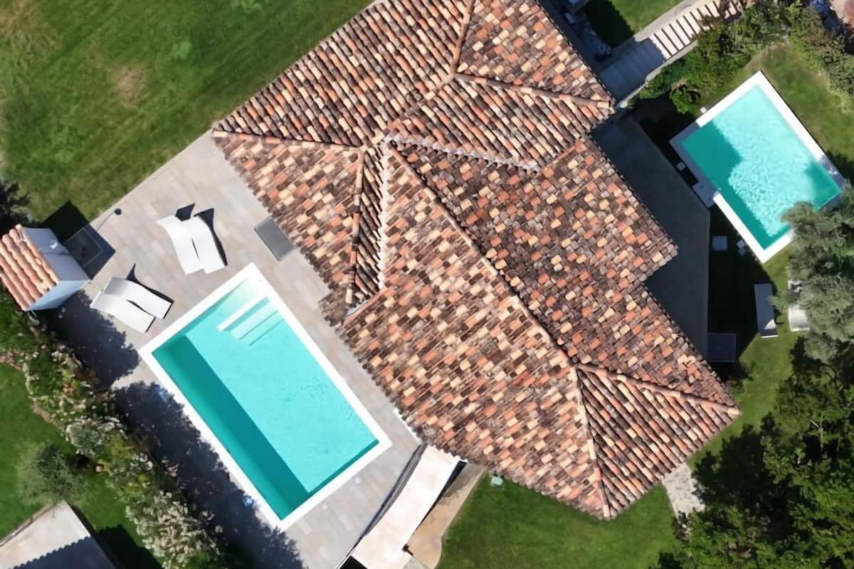 Terraço com telhado de azulejos, duas piscinas e área de pátio com mobiliário de exterior.