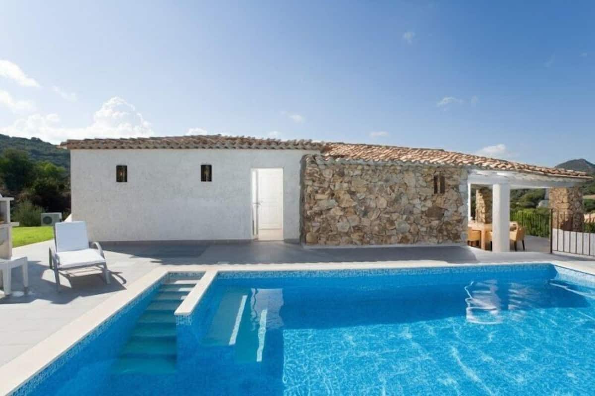 Uma piscina com escadas de acesso, um edifício branco com parede de pedra e uma porta.