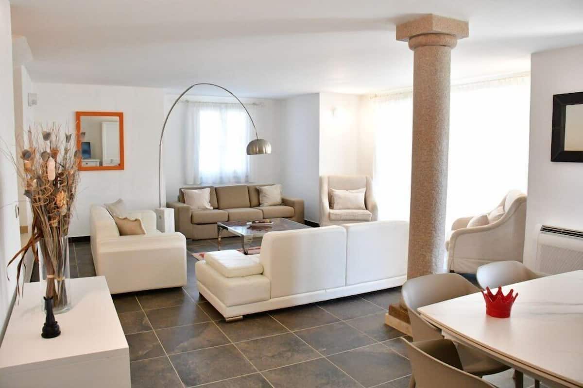 Uma sala de estar moderna com sofá, poltronas, mesa de centro e mesa de jantar.