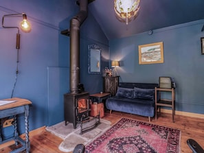 Um quarto com lareira a lenha, um sofá azul, um tapete estampado, uma mesa de madeira e um espelho na parede.