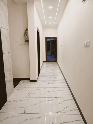 Um corredor com pisos de mármore branco, uma porta no final e um interruptor de luz na parede.