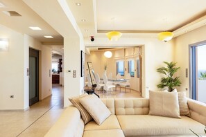 Uma sala de estar moderna com um sofá bege, um espaço de jantar com mesa de vidro e uma janela grande que oferece iluminação natural.