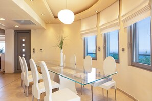 Uma sala de reuniões moderna com mesa de vidro, cadeiras brancas, um vaso de planta e grandes janelas com vista.