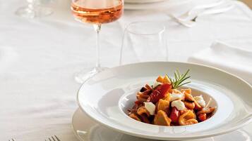 Uma mesa de jantar com um prato de comida, dois copos de vinho e uma saladeira ao fundo.