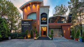 Um hotel com fachada curva, entrada destacada e uma placa com a inscrição 'HOTEL WHISPERING WINDS'.