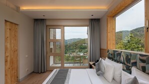 Quarto com uma grande janela, uma cama, uma cadeira e vista para uma paisagem montanhosa.